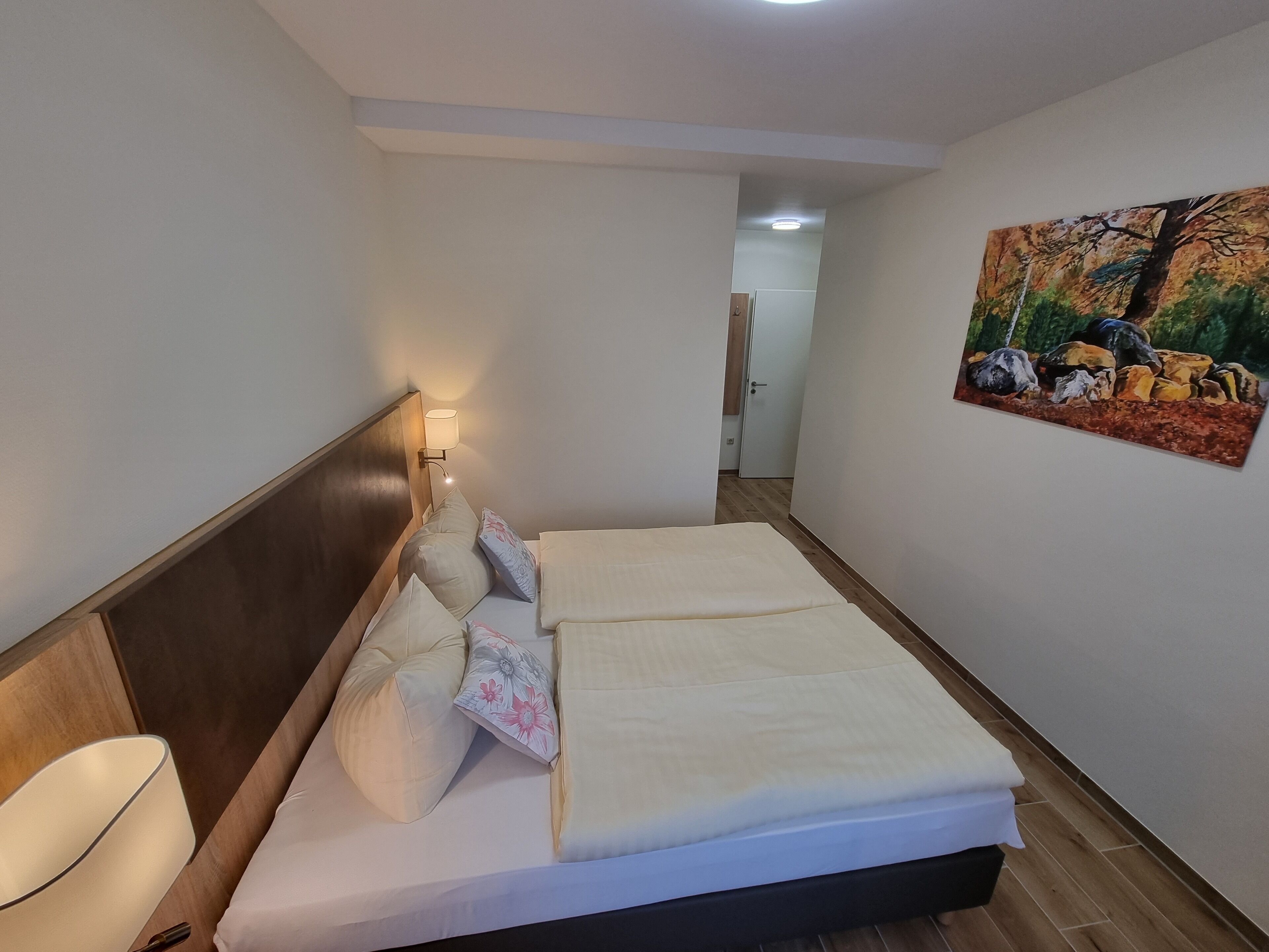 Quarto de hotel com uma cama, mesa de cabeceira, abajur e um quadro na parede.