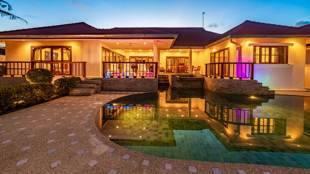 Uma casa de dois andares com piscina, varanda coberta e fachada bem iluminada.