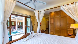 Quarto de hotel com cama, ventoinha no teto, guarda-roupa de madeira e vista para a área da piscina.