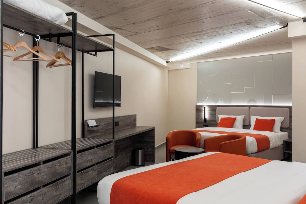 Quarto de hotel moderno com uma cama, duas cadeiras, uma escrivaninha e uma televisão.