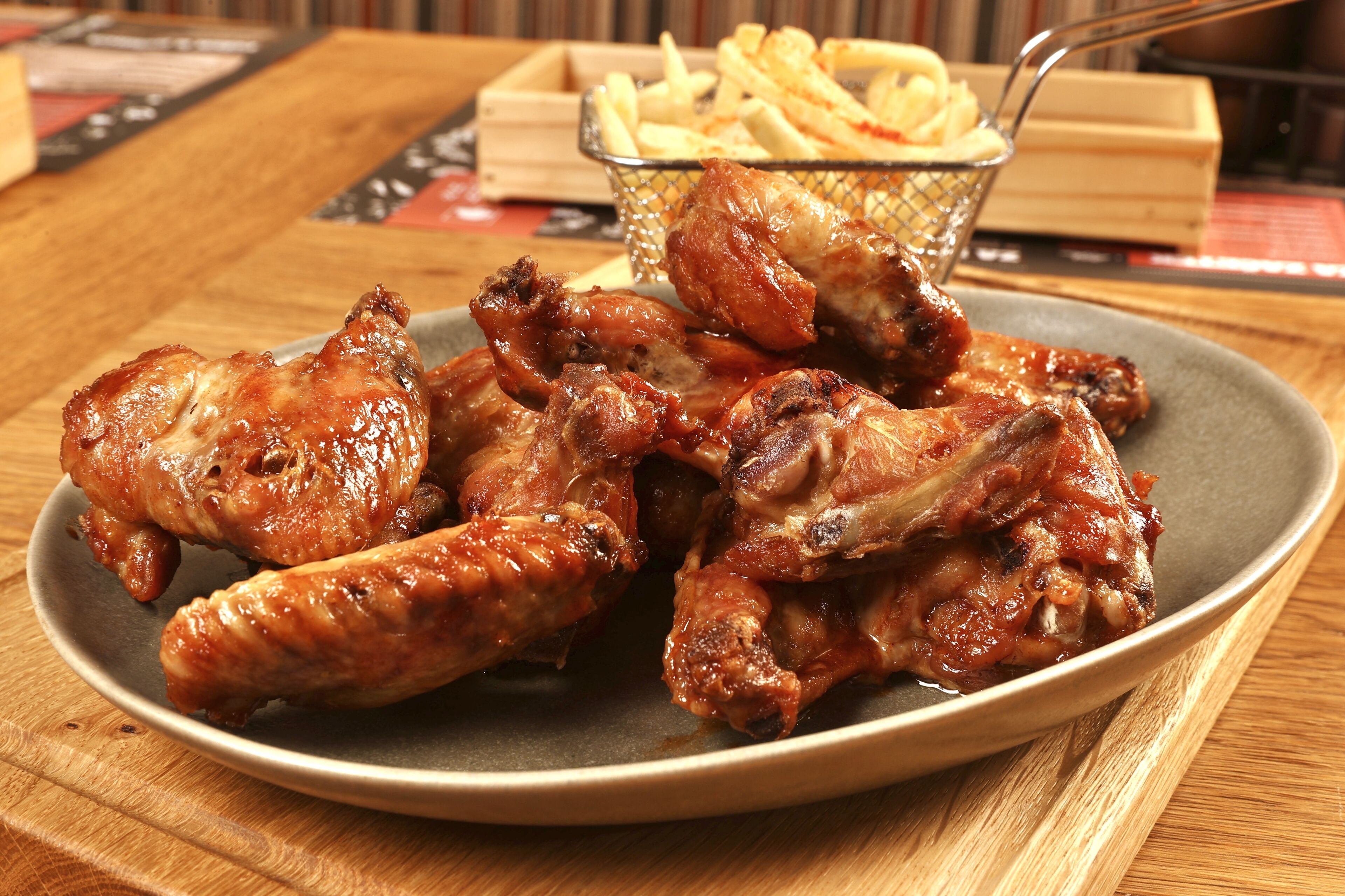 Um prato de asas de frango e um cesto de batatas fritas sobre uma mesa de madeira.