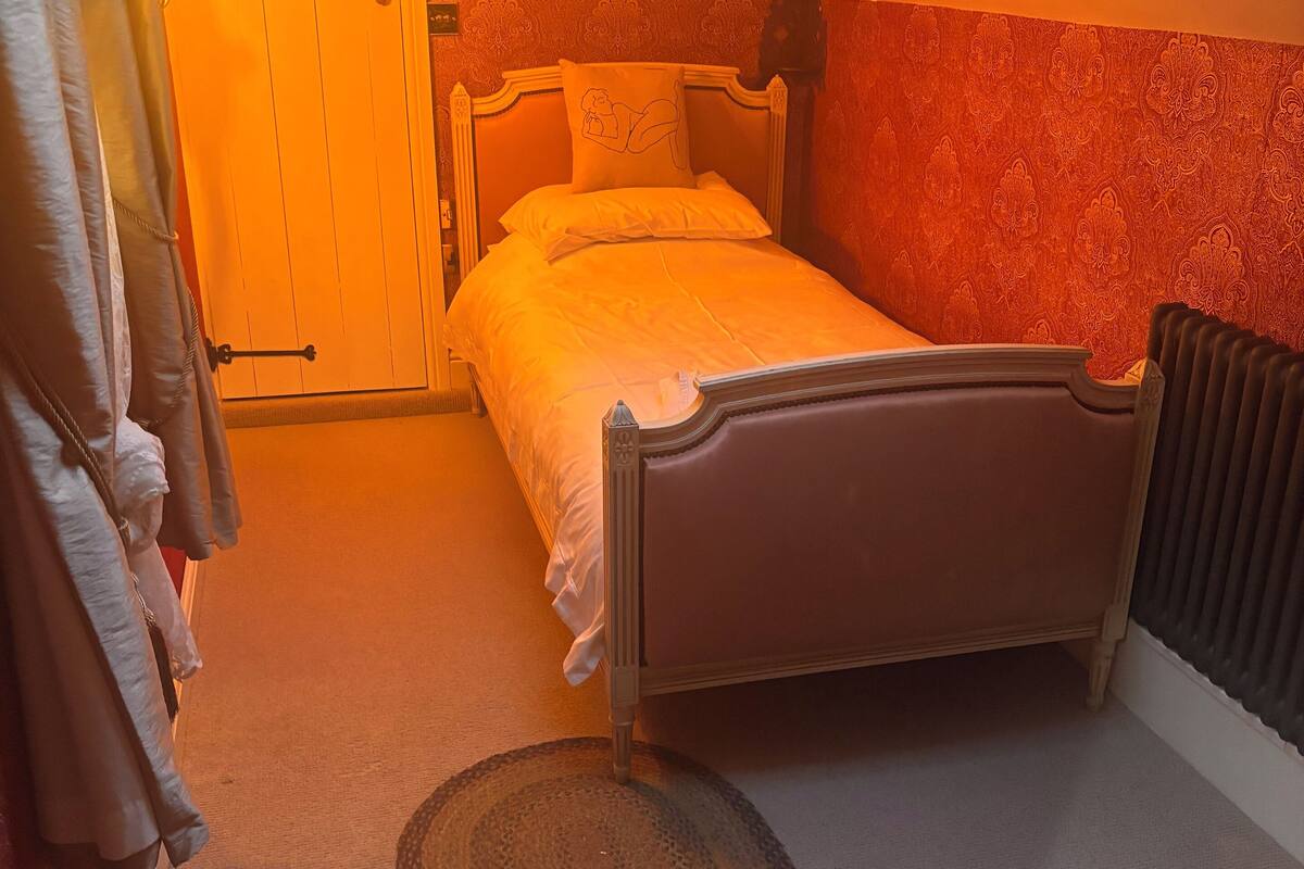 Quarto com cama, radiador, janela e porta.