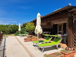 Área externa com assentos de lounge e guarda-sóis, um edifício de pedra e um pátio com azulejos.