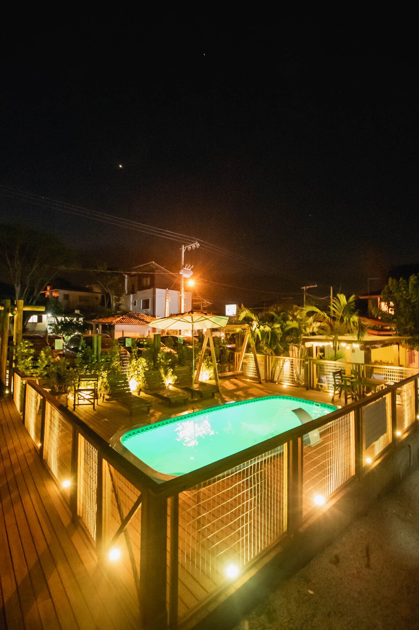 Uma banheira de hidromassagem cercada por um deck de madeira com cerca, palmeiras e uma casa ao fundo.