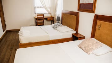 Quarto de hotel com duas camas, uma escrivaninha e uma cadeira.