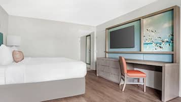 Quarto de hotel moderno com uma cama grande, uma escrivaninha com cadeira, televisão de tela plana e vista para o mar.