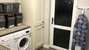 Uma lavanderia com máquina de lavar, cestos empilhados e uma porta com painel de vidro jateado.