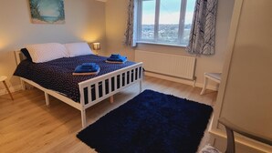 Quarto com cama, janela com cortinas, radiador e um quadro na parede.