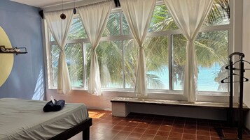 Quarto com cama, um banco e amplas janelas com cortinas.