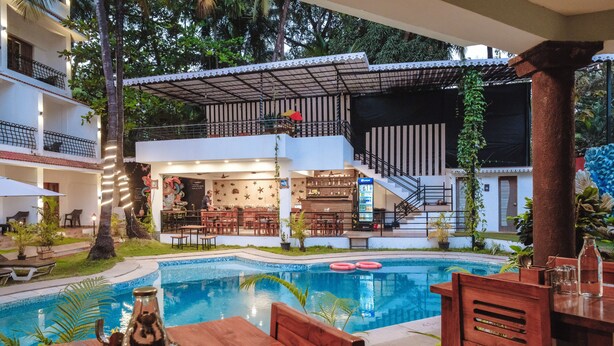 Uma área à beira da piscina com bar, assentos externos e escada para um andar superior.