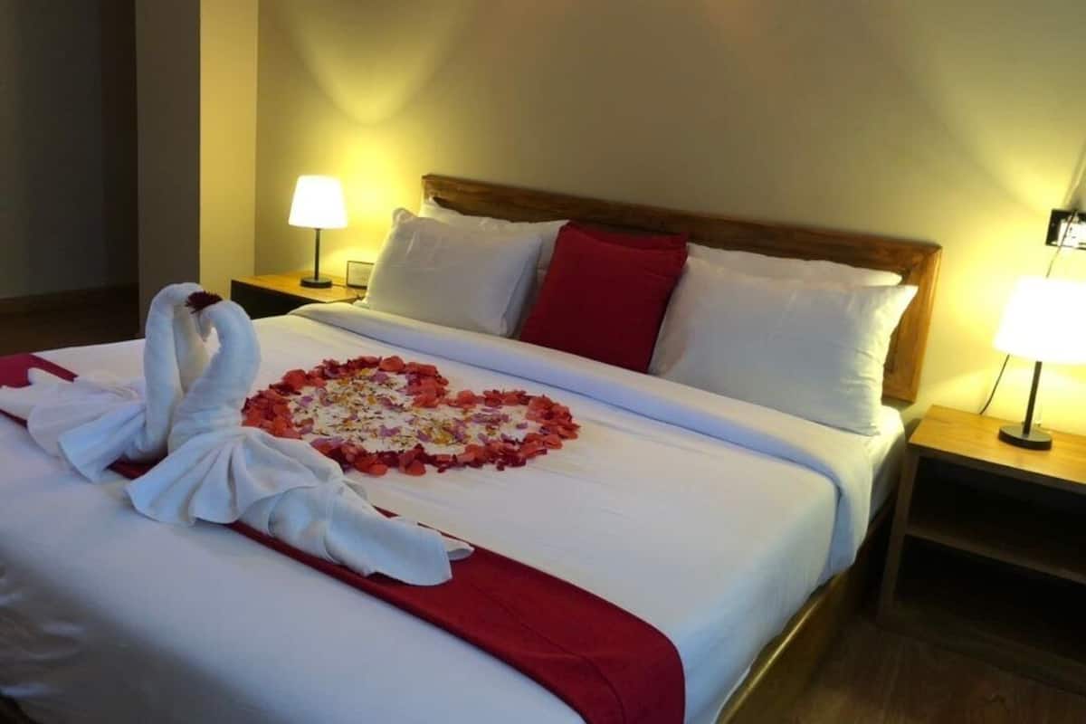Uma cama bem arrumada com um arranjo de flores em formato de coração e duas toalhas dobradas em cisnes.