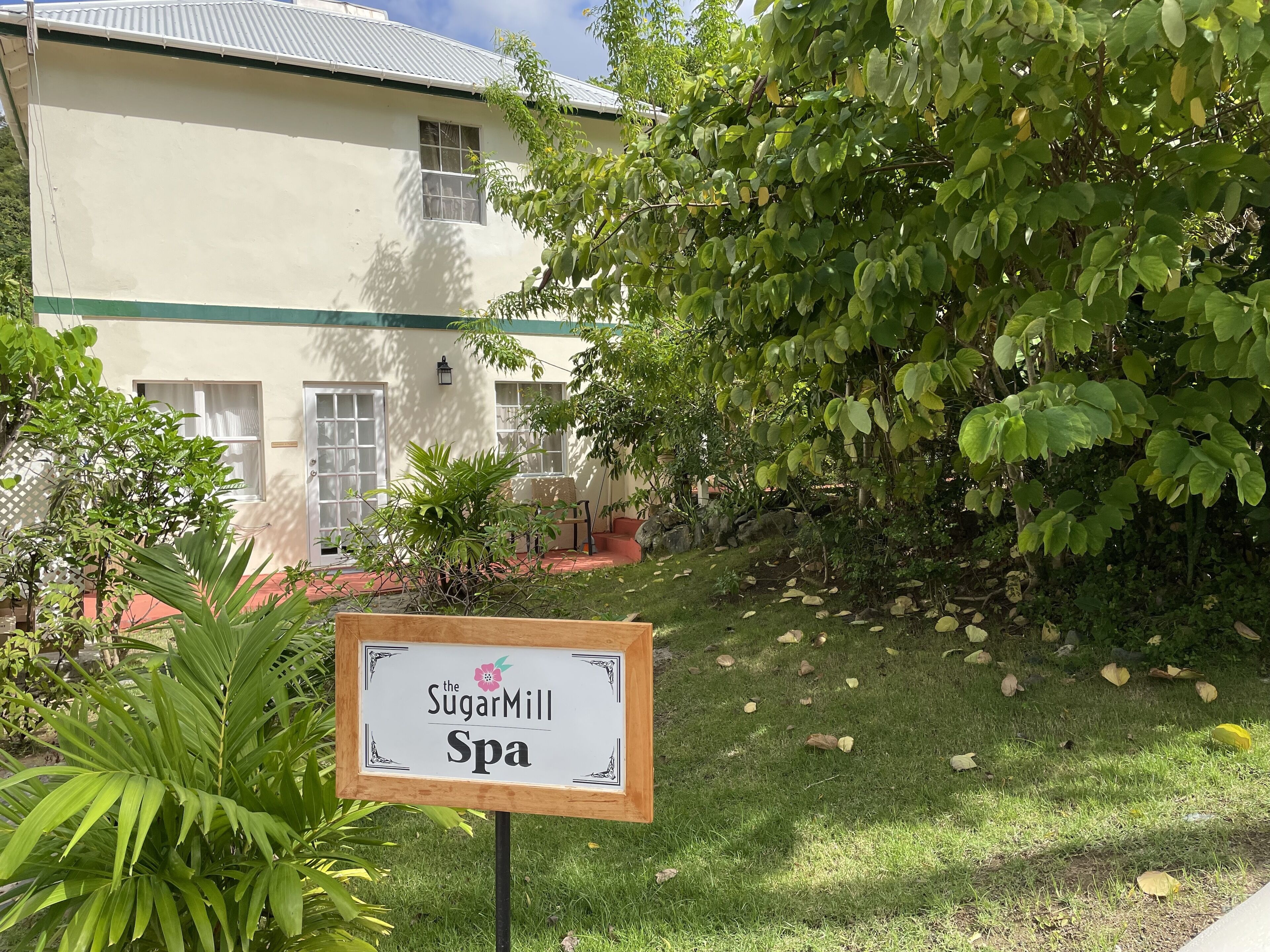 Placa para 'The SugarMill Spa' em área de jardim, com um edifício ao fundo.
