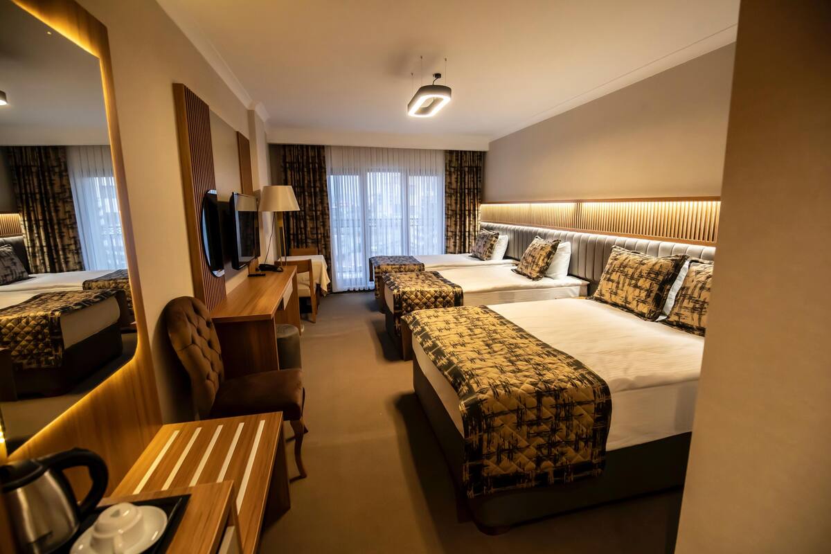 Quarto de hotel com duas camas, uma escrivaninha, uma cadeira, uma televisão e um espelho grande.