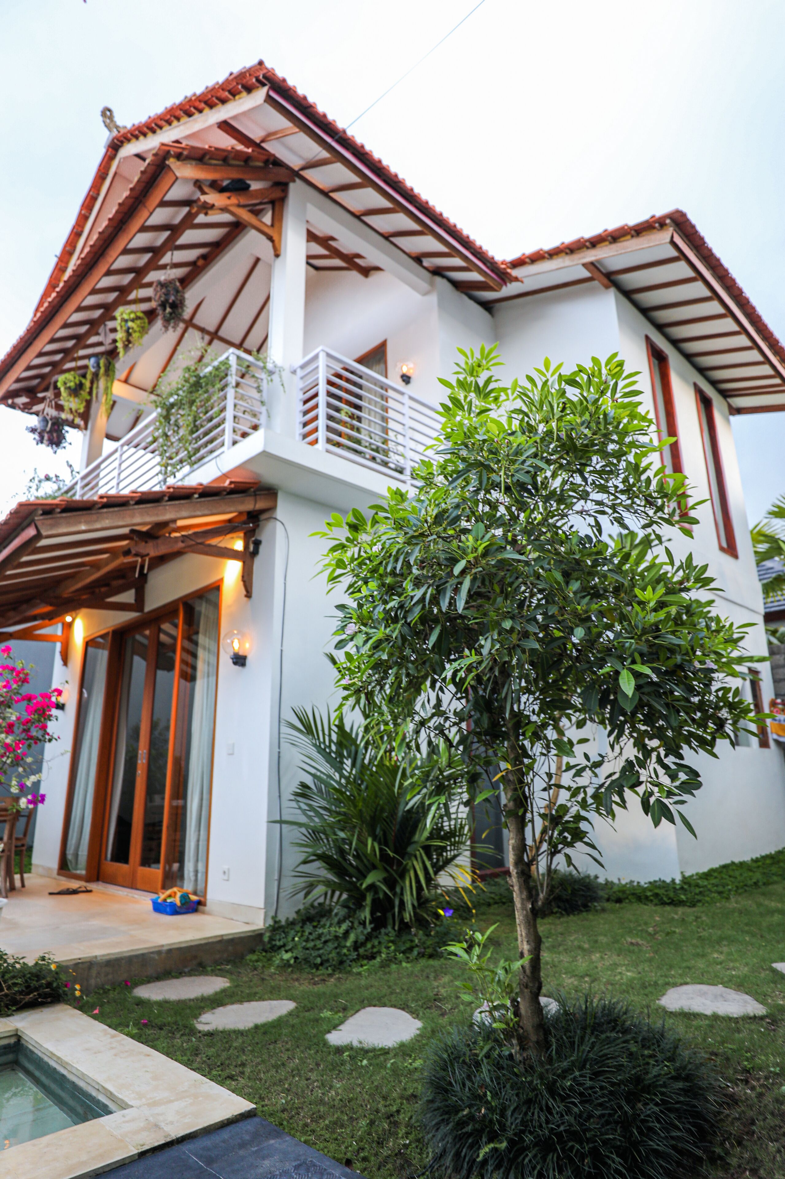 Uma casa de dois andares com varanda, um pequeno jardim com pedras para caminhar e uma piscina.