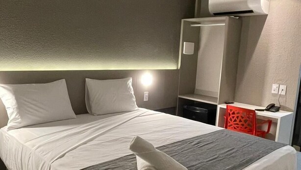 Quarto de hotel com uma cama grande, uma escrivaninha com cadeira, um espelho e um aparelho de ar condicionado.