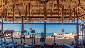 Uma academia com equipamentos de ginástica e vista para o mar.