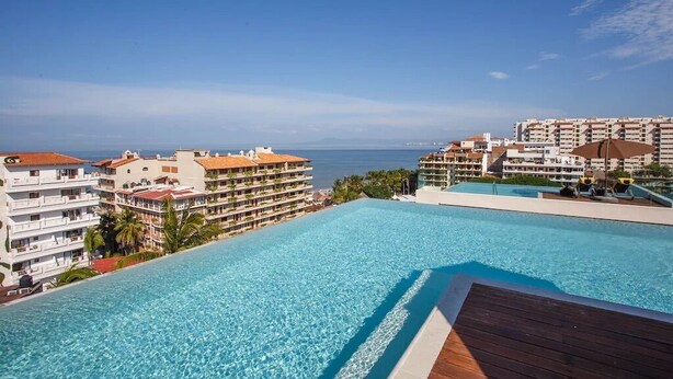 Piscina infinita no terraço com vista para o mar e edifícios ao redor.