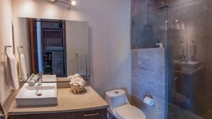Uma casa de banho moderna com um espelho grande, uma sanita, uma pia e uma cabine de duche com parede de vidro.