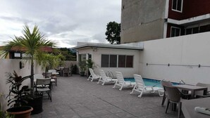 Uma área de estar ao ar livre com espreguiçadeiras, piscina e plantas em vasos.