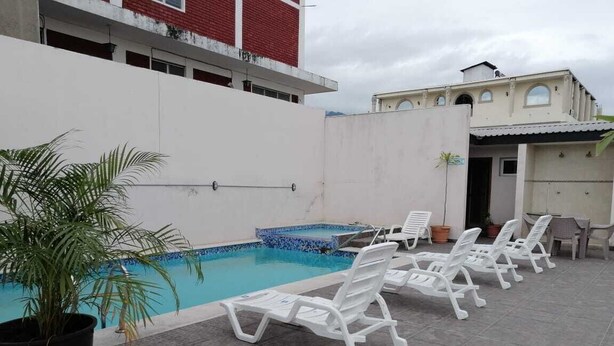 Uma área de piscina no terraço com cadeiras de lounge brancas, uma piscina pequena e plantas em vasos.