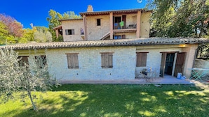 Uma casa de pedra com varanda, um pequeno jardim e uma mesa com cadeiras na área externa.