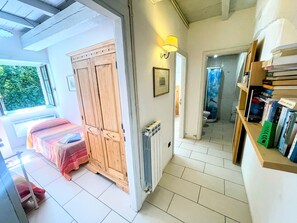 Quarto com uma cama, um guarda-roupa de madeira, radiador, estante de livros e banheiro visível por uma porta aberta.