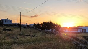 Paisagem rural com um pôr do sol, muros de pedra e edifícios brancos.