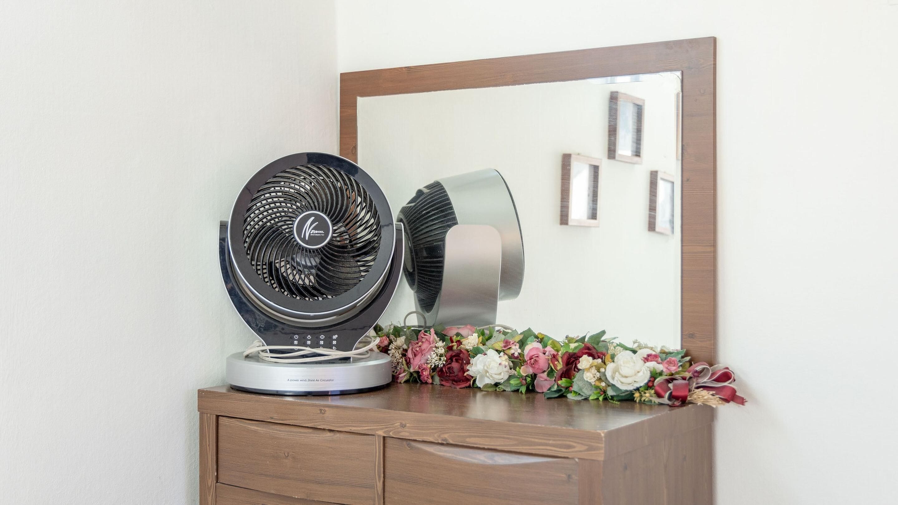 Um ventilador de chão sobre uma cômoda de madeira com um espelho acima.
