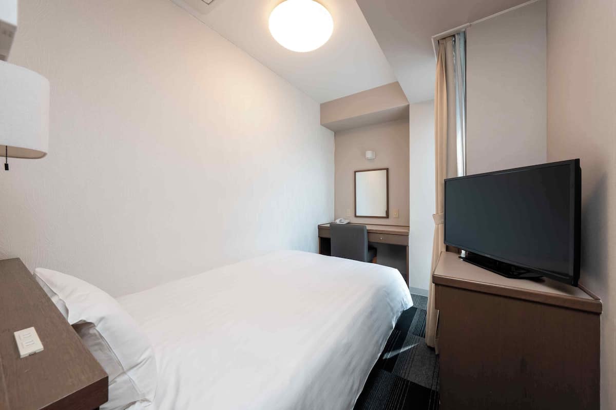 Quarto de hotel com cama, escrivaninha, televisão e espelho.
