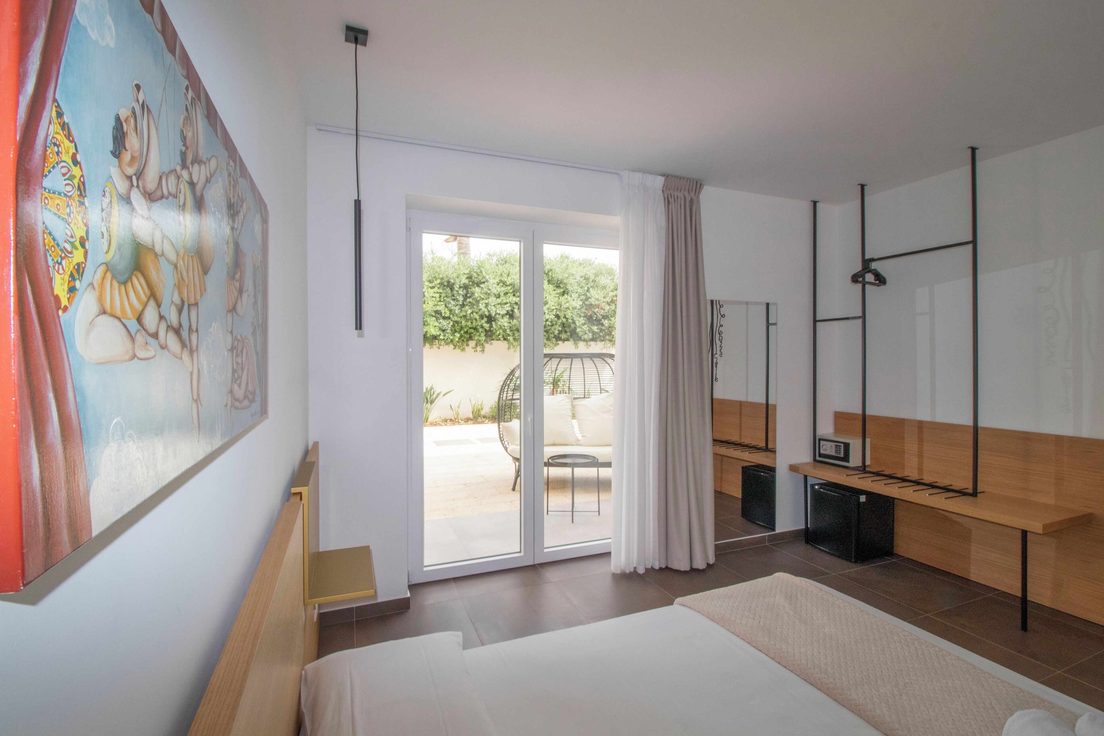 Quarto de hotel com uma cama grande, um banco de madeira, uma pequena mesa, micro-ondas e uma porta de vidro deslizante que dá para uma área externa com uma cadeira e uma mesa.
