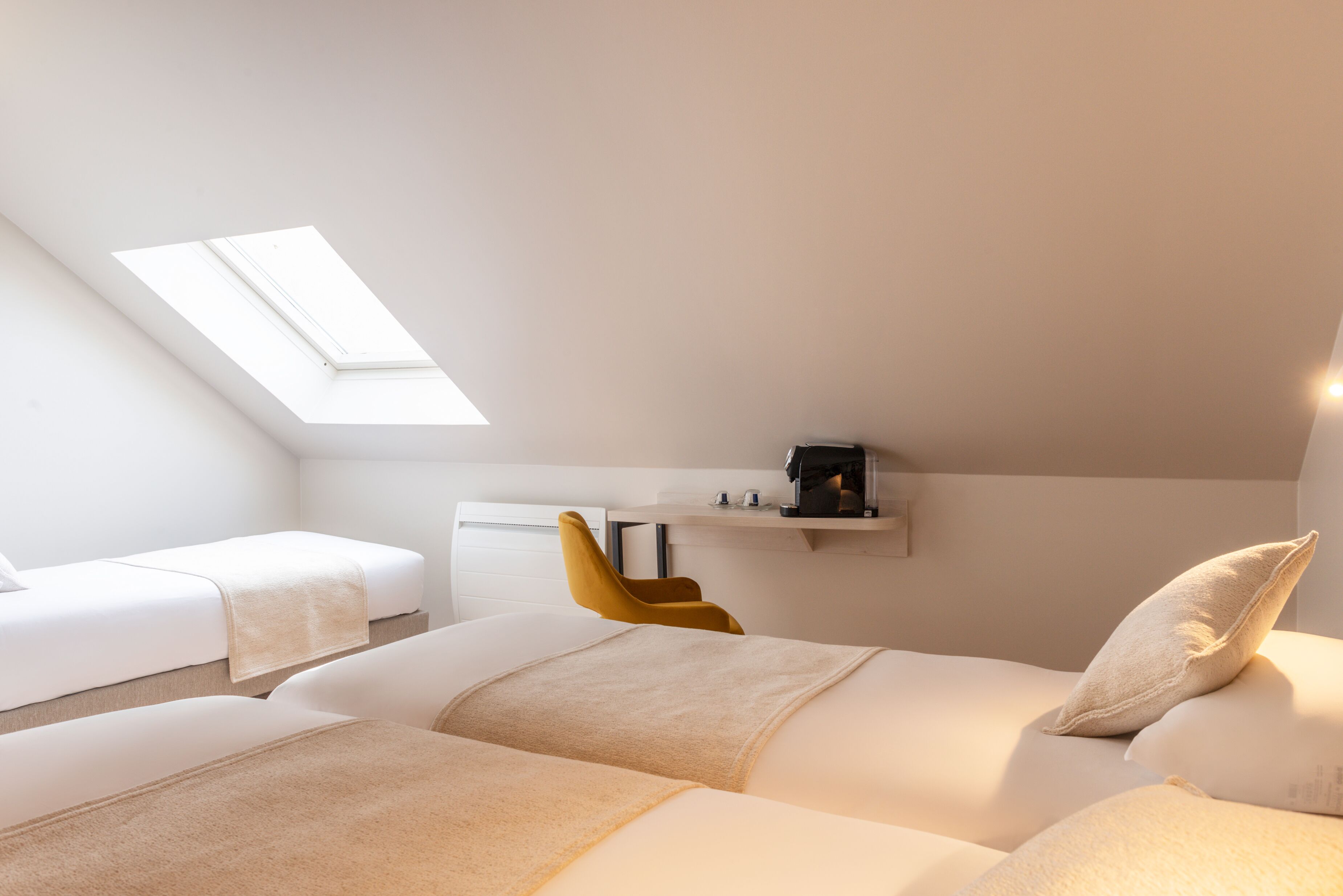 Quarto moderno e bem iluminado, com claraboia, uma cama, uma cadeira e uma prateleira pequena com uma máquina de café.