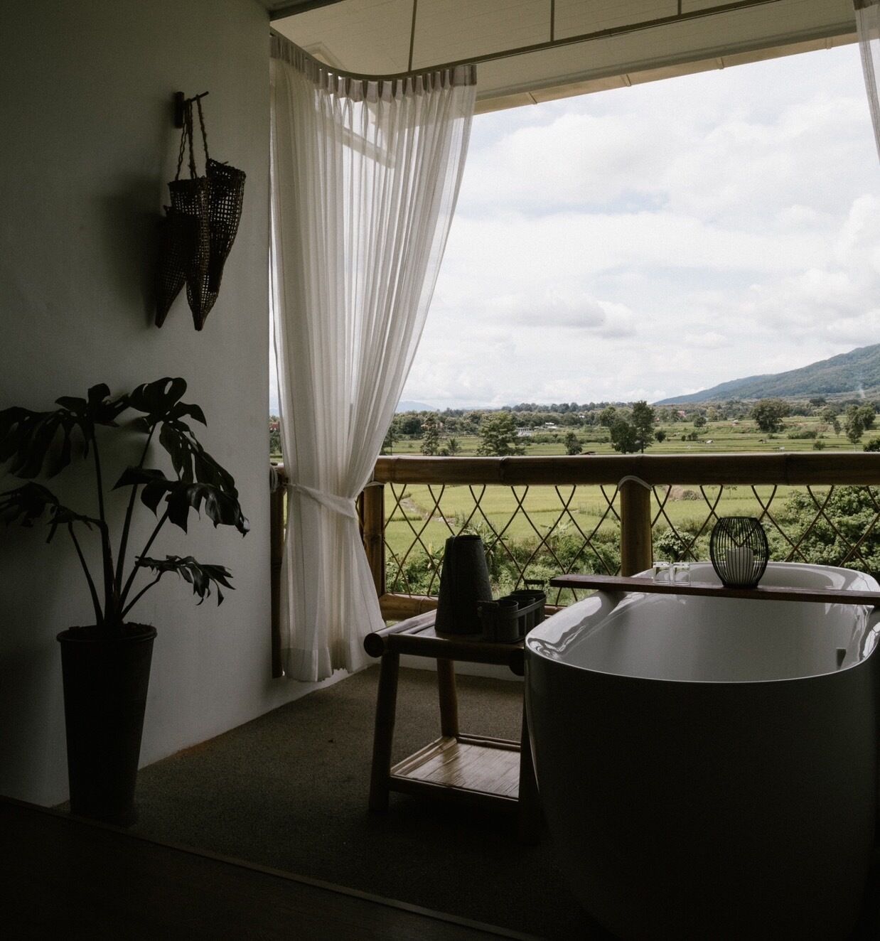 Uma varanda com vista para uma paisagem verde, um vaso de planta, uma cadeira e uma banheira.