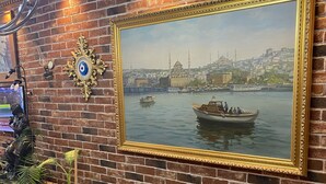 Parede de tijolos com uma grande pintura emoldurada de uma paisagem urbana, um sofá com detalhes em tufos e uma pequena mesa com uma planta.