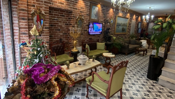 Um hall amplo com parede de tijolos, um candelabro, uma árvore de Natal e uma televisão.