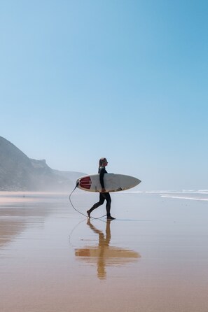 Uma pessoa caminhando na praia segurando uma prancha de surf.