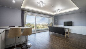 Quarto de hotel moderno com uma varanda ampla, uma televisão e um espaço de refeições com dois banquetes.