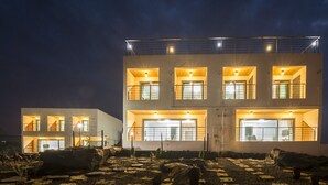 Um edifício moderno de vários andares com várias varandas e grandes janelas, rodeado por um jardim bem cuidado.