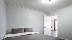 Quarto com cama, porta que dá para outro cômodo e luminária no teto.