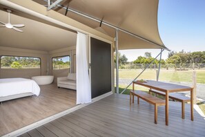 Quarto amplo com uma cama, um sofá, uma mesa de madeira e uma grande porta deslizante que dá para uma área externa.