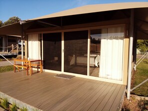 Uma área externa coberta com um deck de madeira, uma mesa e um banco.