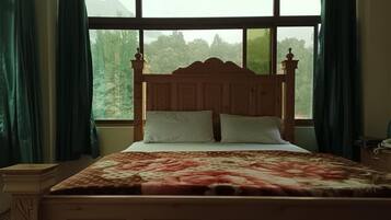Uma cama com colcha florida, cabeceira de madeira e vista para árvores através de uma janela.