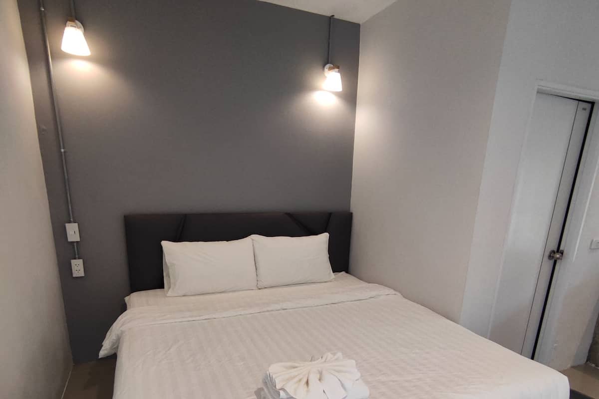 Quarto de hotel moderno com uma cama grande, duas luminárias de cabeceira e uma cama bem arrumada com uma toalha dobrada.