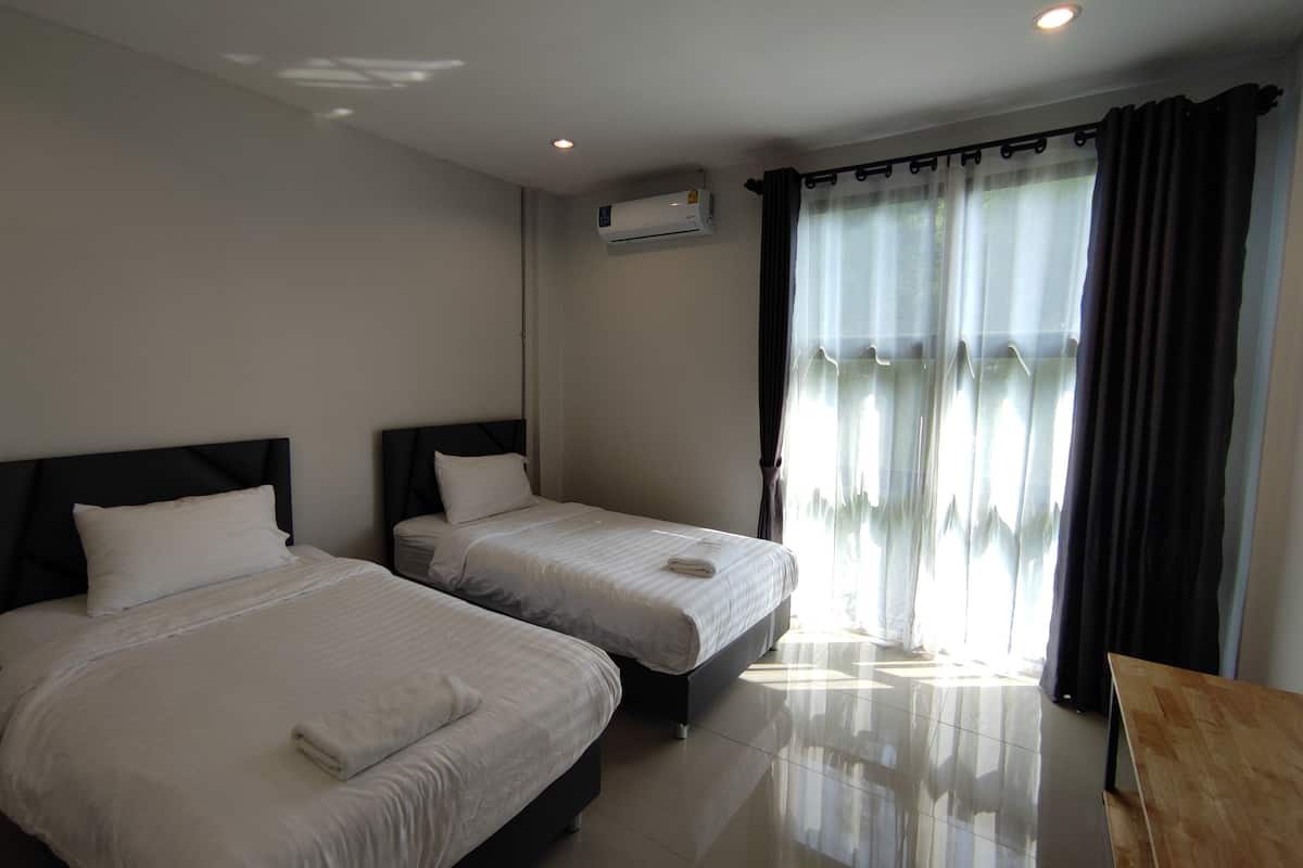 Quarto de hotel com duas camas, uma mesa de madeira e uma janela com cortinas.