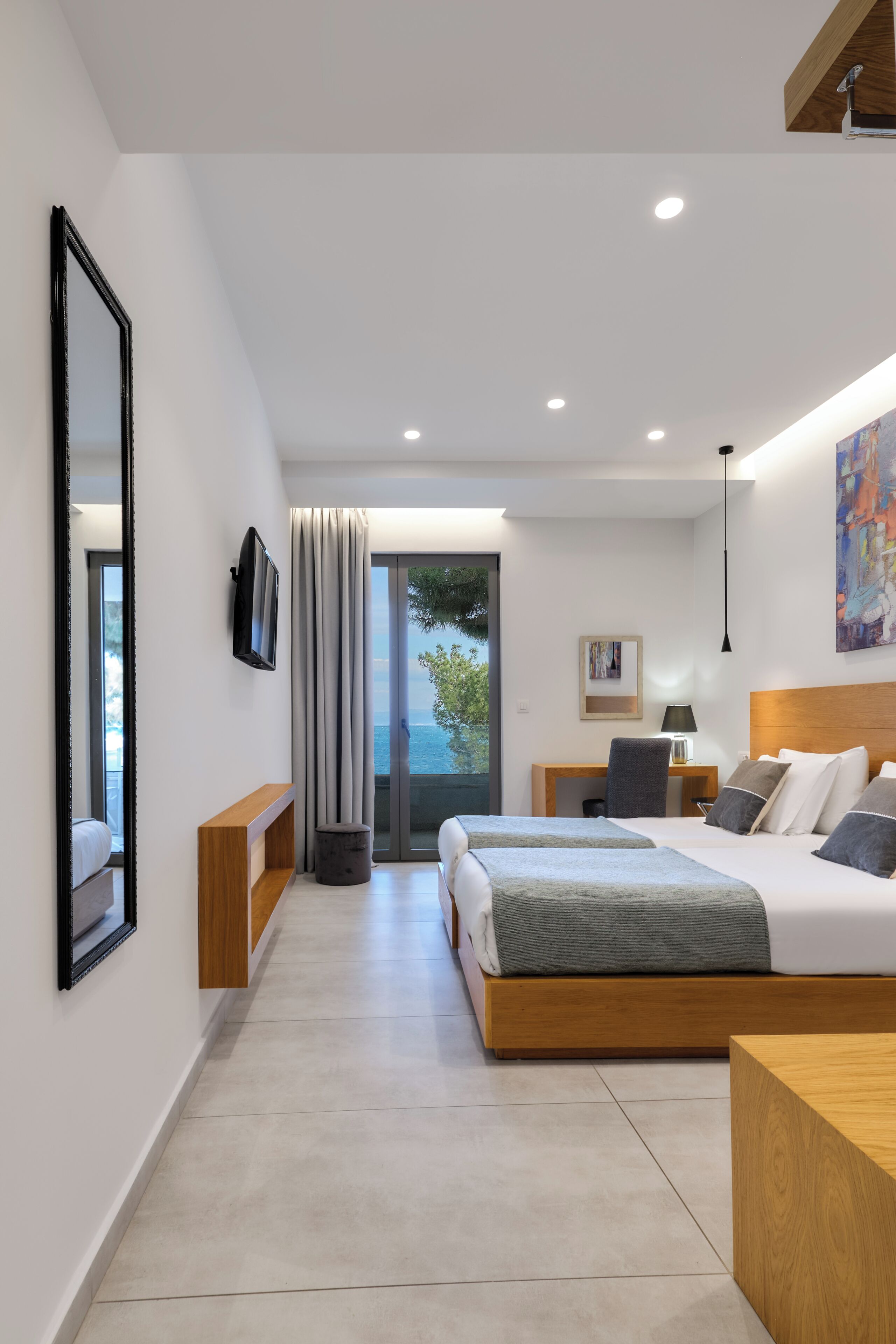Quarto de hotel moderno com uma cama grande, uma escrivaninha, uma cadeira, uma TV e vista para o mar.