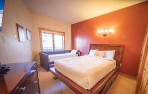 Quarto com cama grande, cômoda, janela e luminária fixada na parede.