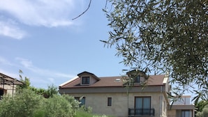 Uma casa de dois andares com piscina, rodeada por vegetação e um muro de pedra.