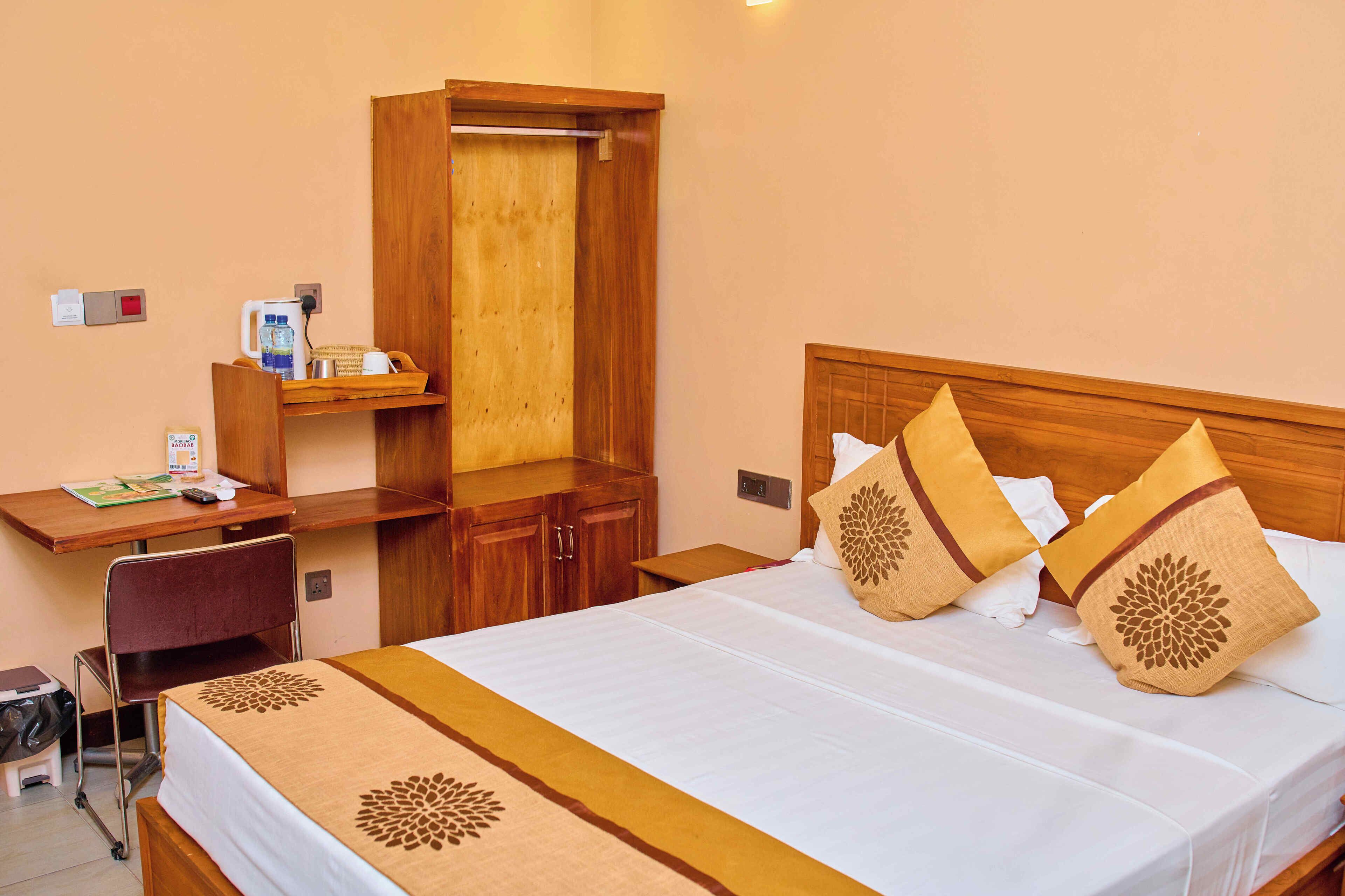 Quarto de hotel com cama, escrivaninha, cadeira e guarda-roupa.