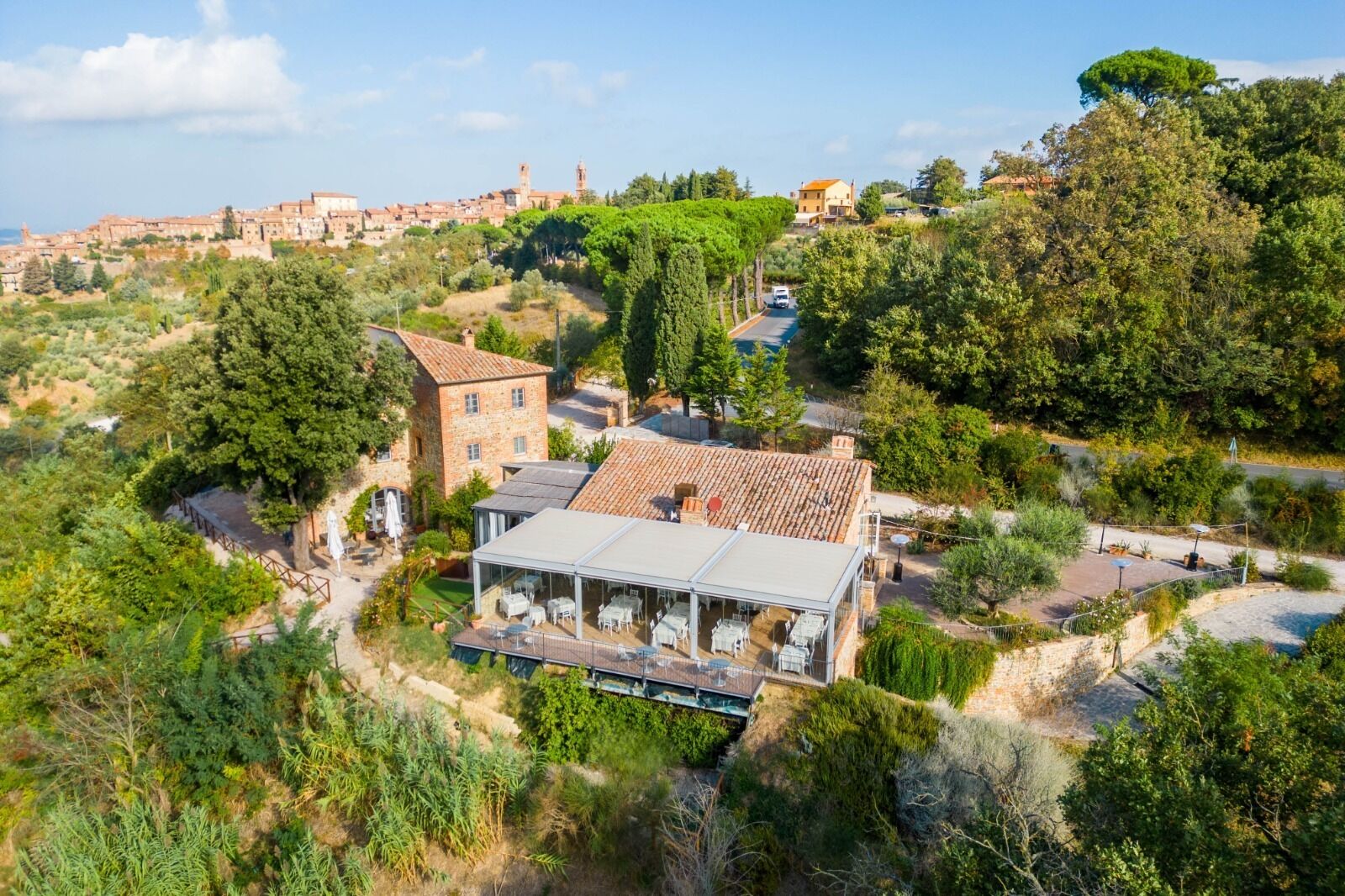 Uma villa com terraço, rodeada por vegetação exuberante e uma vila na encosta ao fundo.
