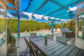 Um pátio externo com mesa, cadeiras, churrasqueira e piscina.