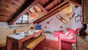 Quarto de sótão com teto de madeira, mesa de jantar posta com pratos e copos, sofá vermelho e televisão.